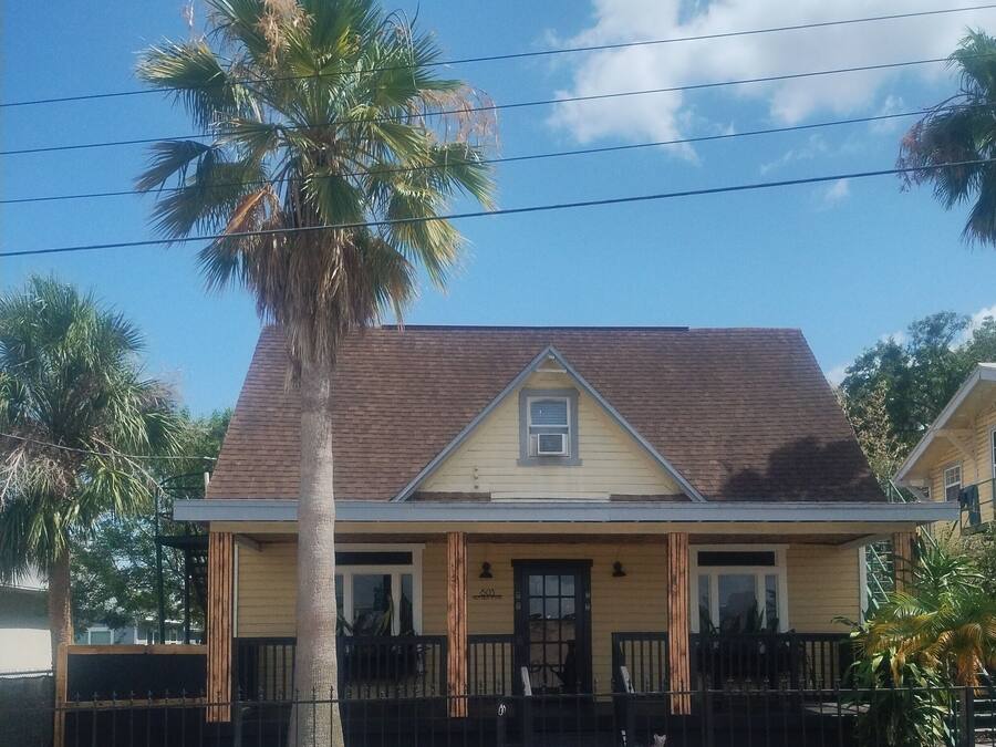 Uma casa amarela térrea com telhado em duas águas, varanda frontal e quintal cercado.