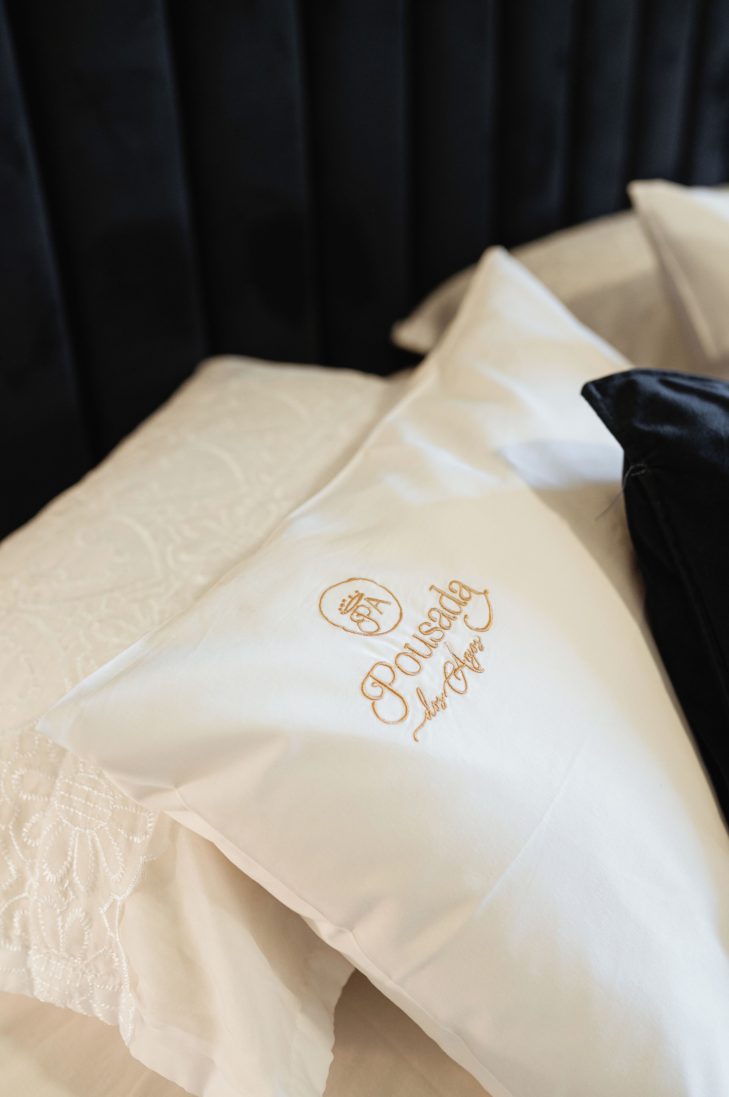 Uma cama com um travesseiro branco com bordado e um travesseiro preto.