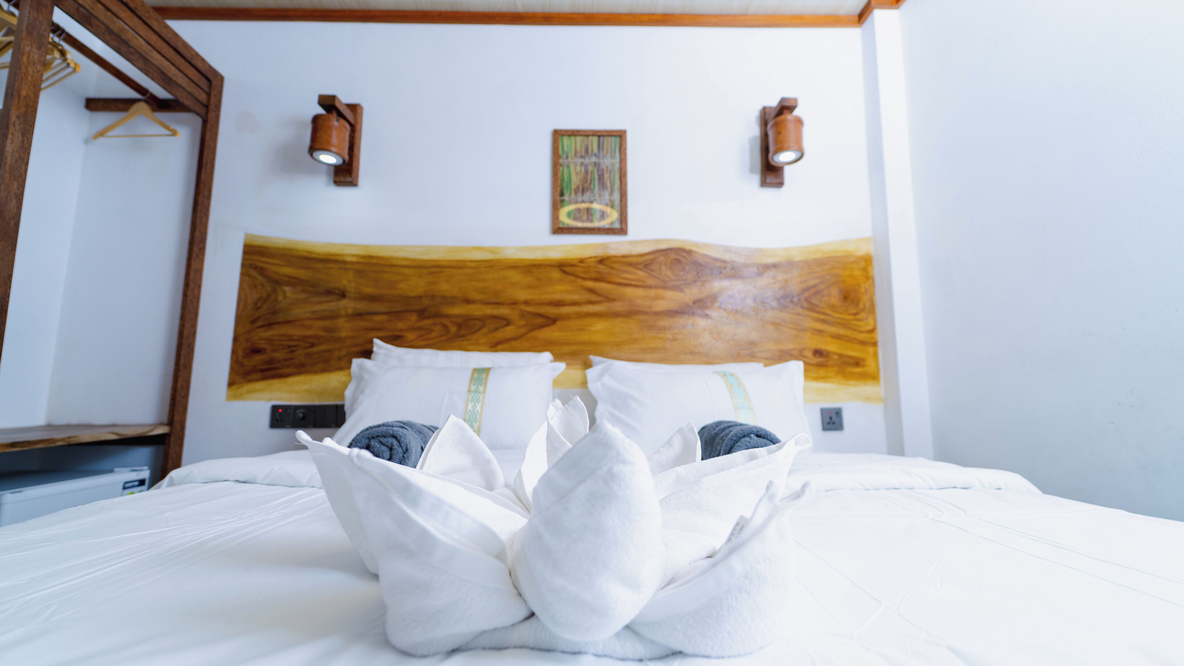 Quarto de hotel com cabeceira de madeira, cama com roupa de cama branca e duas luminárias fixadas na parede.