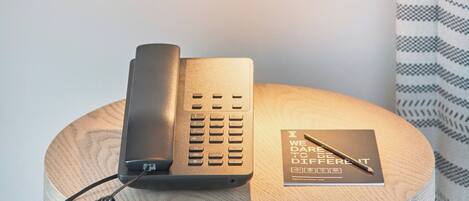 Uma mesa redonda de madeira com um telefone, um interruptor de luz na parede e uma tomada elétrica.