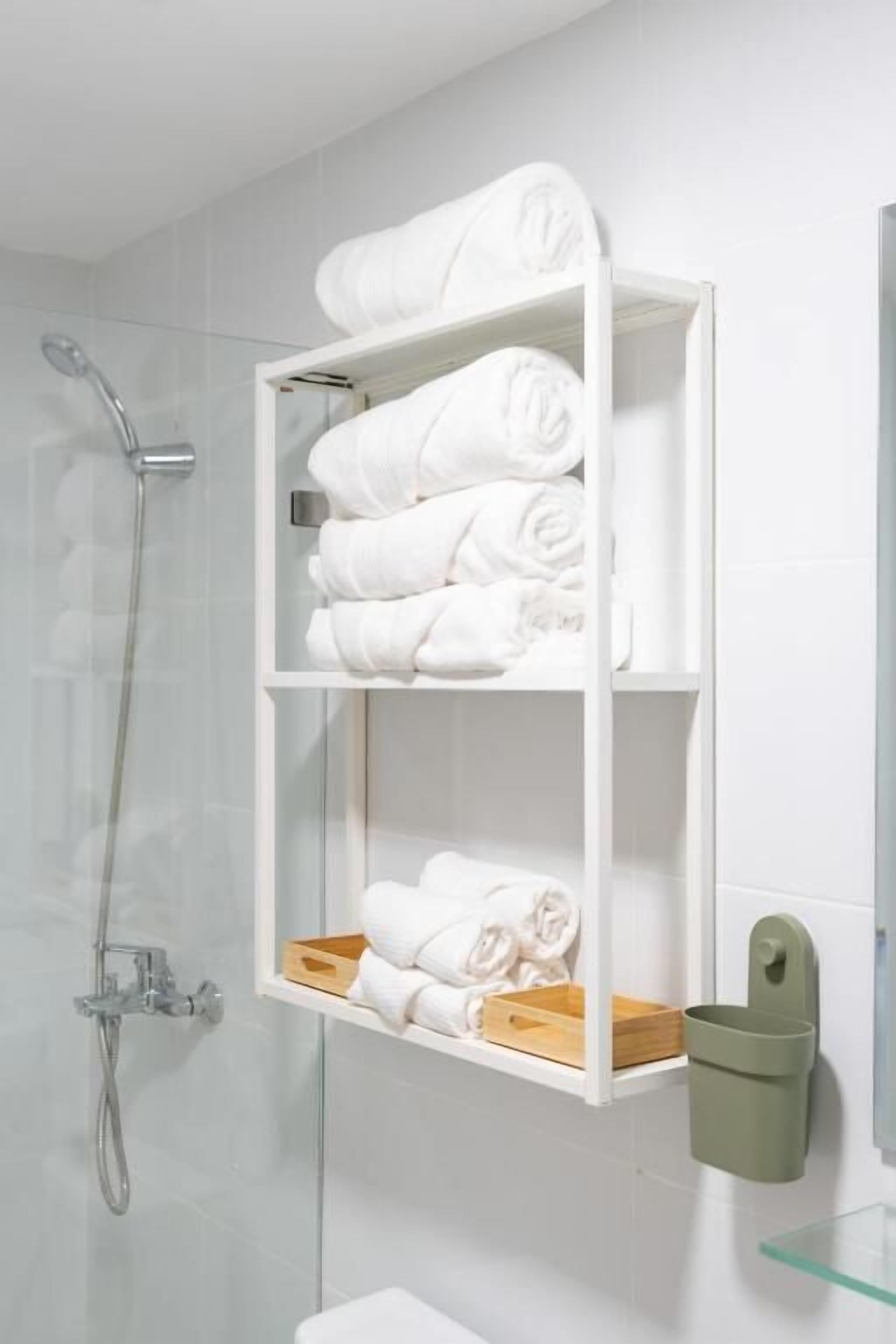 Casa de banho com cabine de chuveiro em vidro, um porta-toalhas branco com toalhas e um dispensador de sabonete verde.