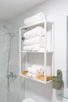 Casa de banho com cabine de chuveiro em vidro, um porta-toalhas branco com toalhas e um dispensador de sabonete verde.