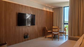 Uma sala de estar moderna com uma televisão de tela plana na parede, uma mesa redonda com cadeiras e uma grande janela com cortinas.
