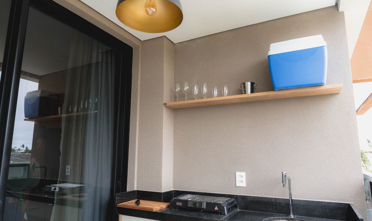 Uma cozinha moderna com bancada preta, prateleira de madeira com copos e um recipiente, e um cooler azul.