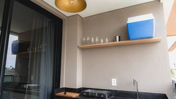 Uma cozinha moderna com bancada preta, prateleira de madeira com copos e um recipiente, e um cooler azul.