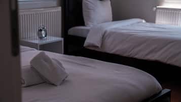 Quarto de hotel com duas camas, uma mesa de cabeceira com relógio e um radiador.