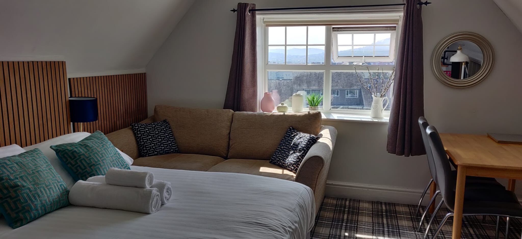 Quarto de hotel acolhedor com cama, sofá, secretária e janela com cortinas.