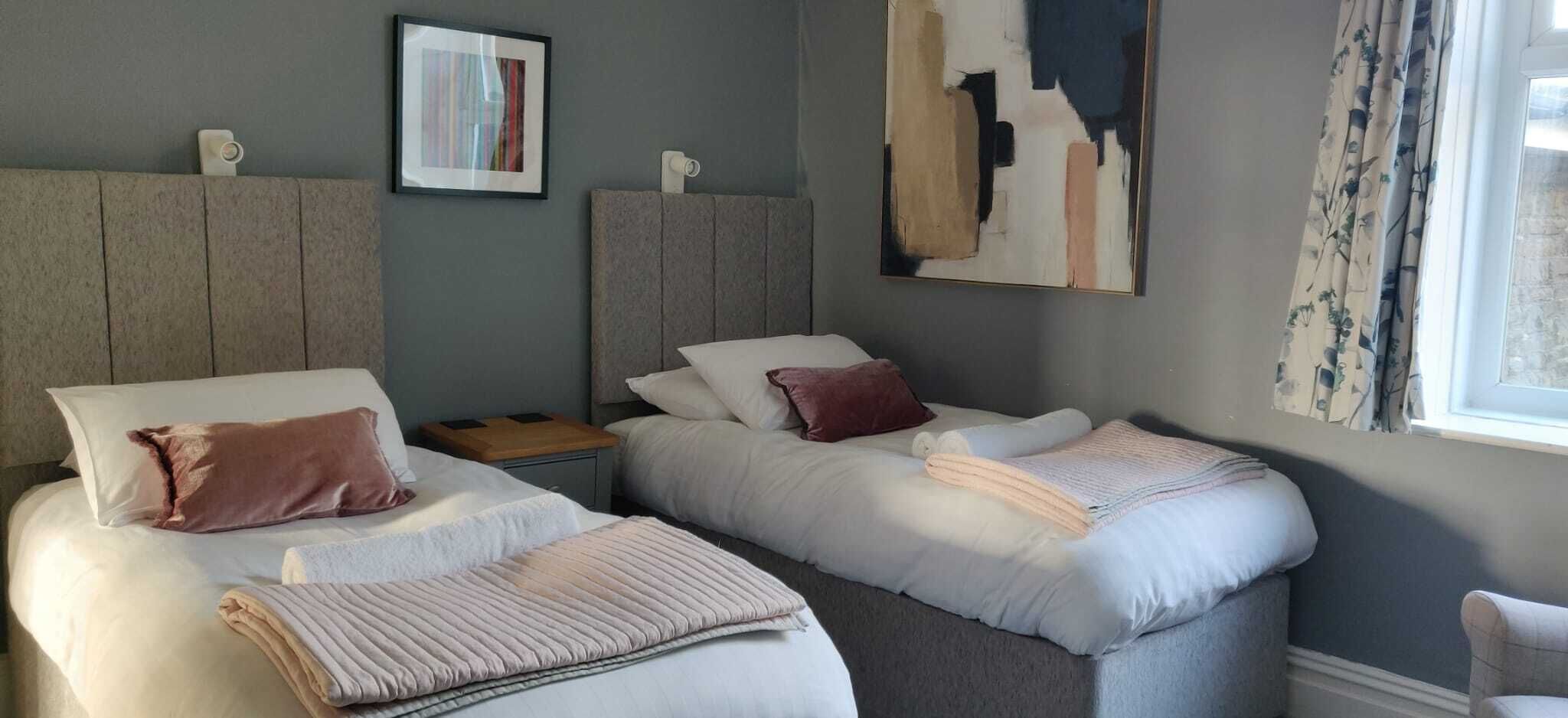 Quarto de hotel com duas camas, uma mesa de cabeceira e obras de arte nas paredes.