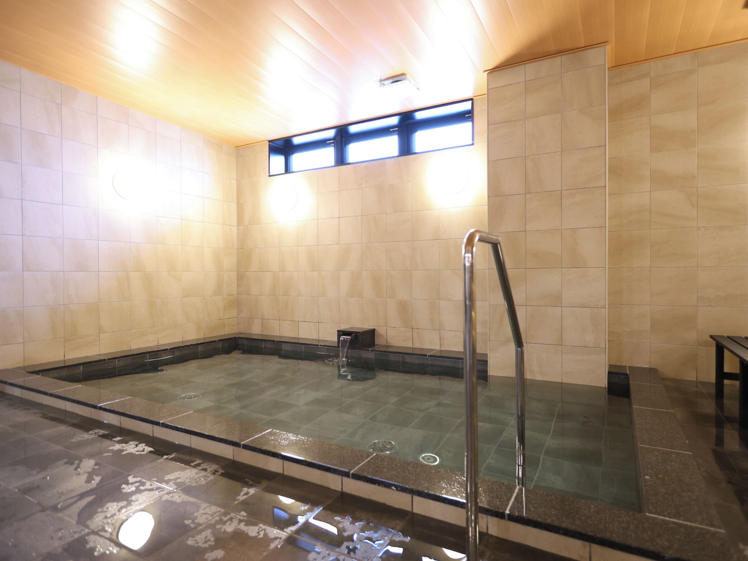 Uma grande piscina interior com barreira de vidro, paredes azulejadas e teto de madeira.