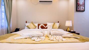 Quarto de hotel com uma cama bem arrumada, arranjo de toalhas em formato de coração, abajur e uma moldura na parede.