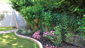 Um jardim ajardinado com uma bordadura de pedra curva, gramado e uma variedade de plantas, incluindo flores cor-de-rosa e folhagem verde.