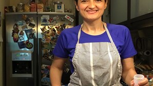 Uma bancada de cozinha com diversos doces e uma pessoa de avental preparando comida.