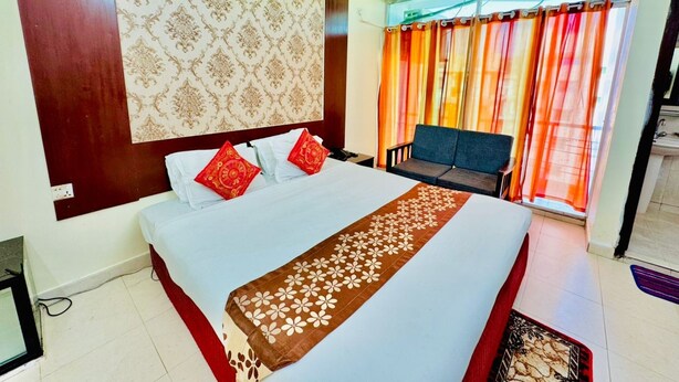 Quarto de hotel com uma cama grande, um sofá, uma TV e uma janela com cortinas.