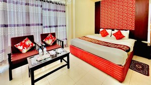 Quarto de hotel com uma cama, uma cadeira, uma mesa com objetos e uma janela com cortinas.