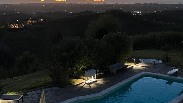 Piscina com espreguiçadeiras e mesa, cercada por um jardim ajardinado.