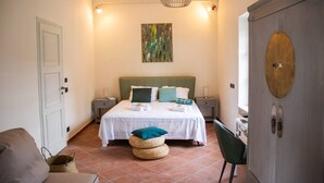 Um quarto com cama, mesas de cabeceira, luminária pendente, pintura na parede e guarda-roupa.