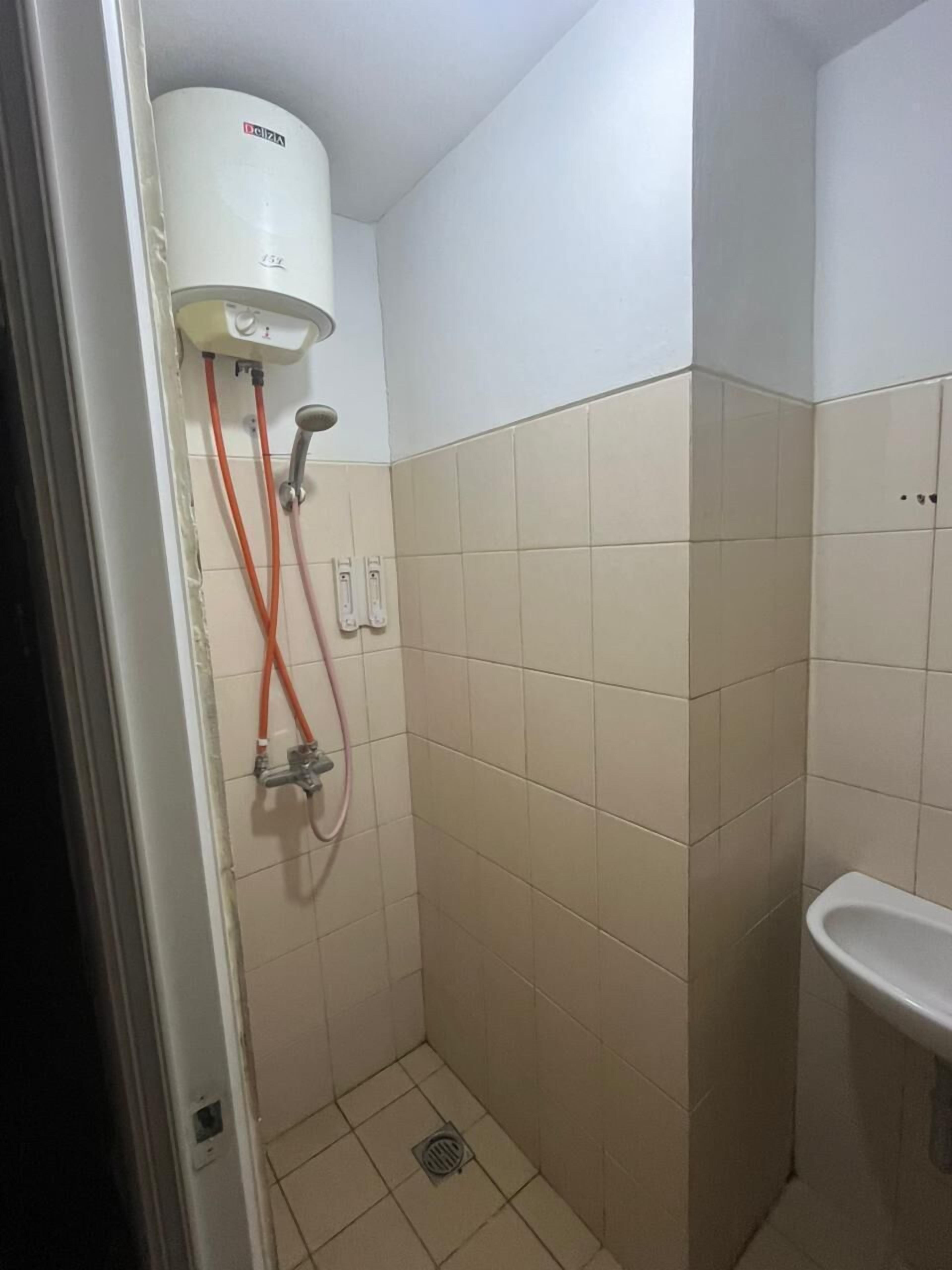 Um banheiro pequeno, com azulejos, tendo um aquecedor pedestal branco, uma pia e um chuveiro com duas mangueiras.
