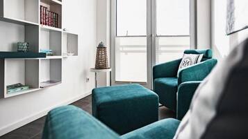 Uma sala de estar moderna com cadeiras estofadas em tons de verde-água, uma estante branca e uma janela grande.