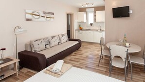Quarto de hotel moderno com sofá, cama, mesa de jantar com cadeiras, cozinha e televisão de tela plana na parede.