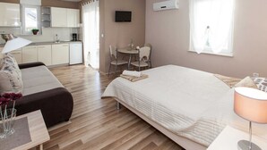 Quarto de hotel moderno com uma cama, um sofá, uma pequena mesa de jantar e uma cozinha compacta.
