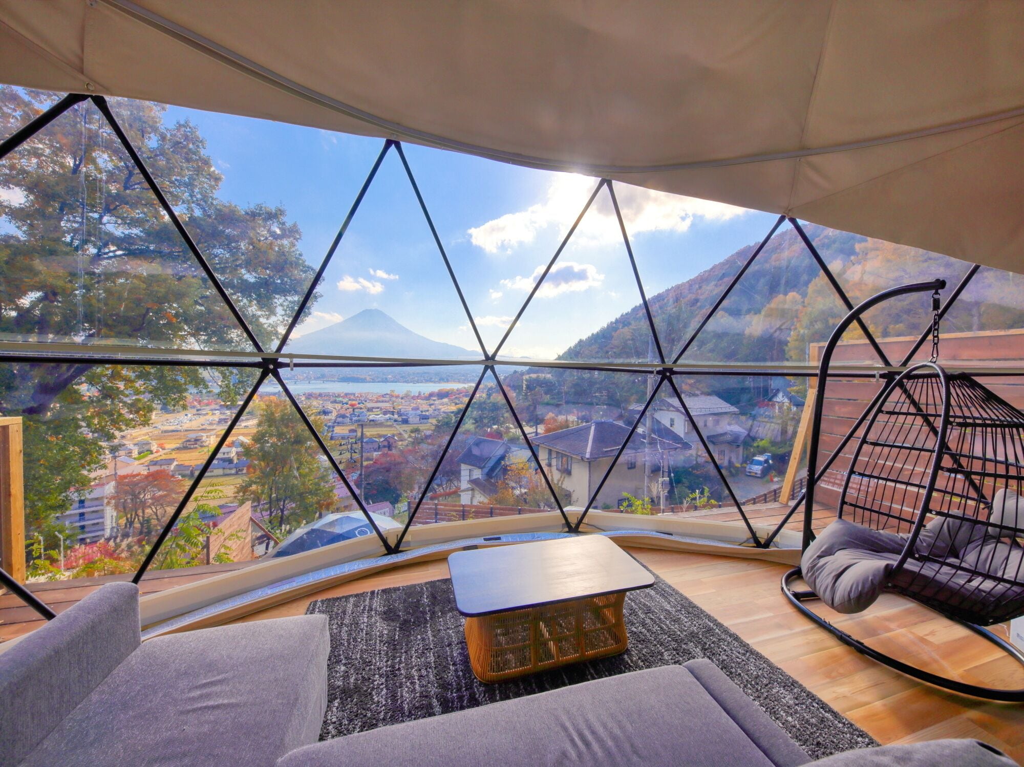Quarto com vista para uma montanha e uma cidade. Possui um sofá, uma mesa pequena e uma cadeira suspensa.