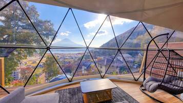 Quarto com vista para uma montanha e uma cidade. Possui um sofá, uma mesa pequena e uma cadeira suspensa.
