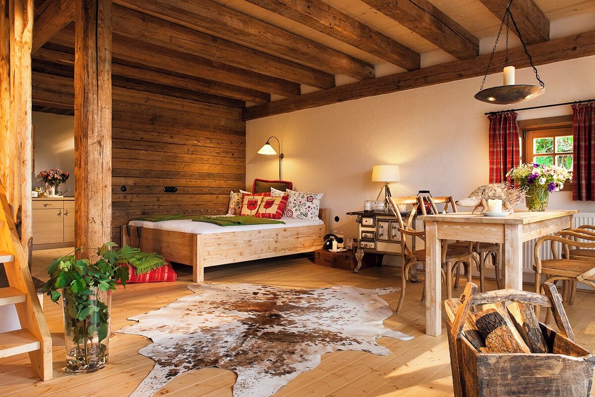 Interior rústico de cabana com cama de madeira, mesa de jantar e tapete de couro.