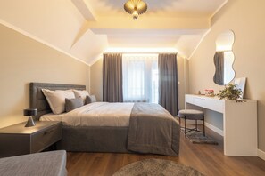 Quarto moderno com cama, mesas de cabeceira, escrivaninha, espelho e janela com cortinas.