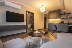 Uma sala de estar moderna com televisão de tela plana, uma mesa redonda pequena com uma planta e um sofá.