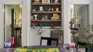 Uma área de refeições com uma mesa posta para refeição, rodeada por cadeiras. Há prateleiras acima da mesa exibindo diversos objetos.