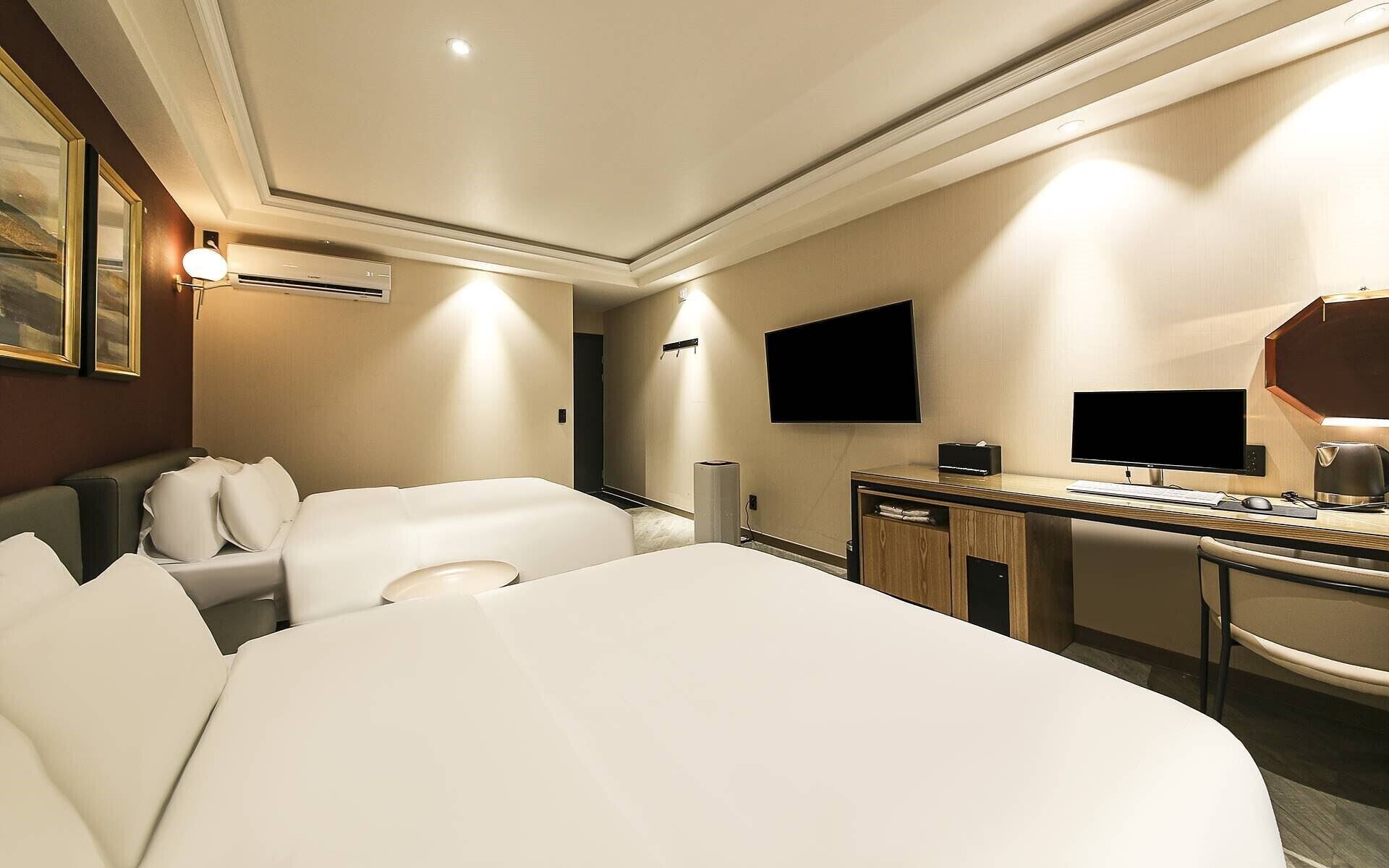 Quarto de hotel com duas camas, uma mesa de escritório com computador, televisão de tela plana e uma janela grande.