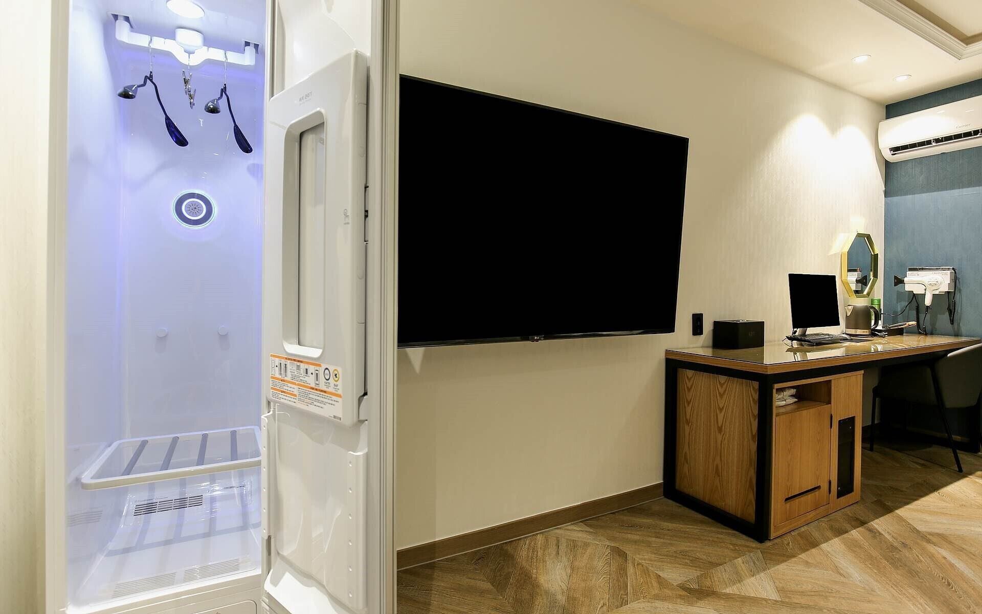 Quarto de hotel moderno com uma televisão de tela grande fixada na parede, um armário de madeira com espelho e um aparelho de ar condicionado instalado.
