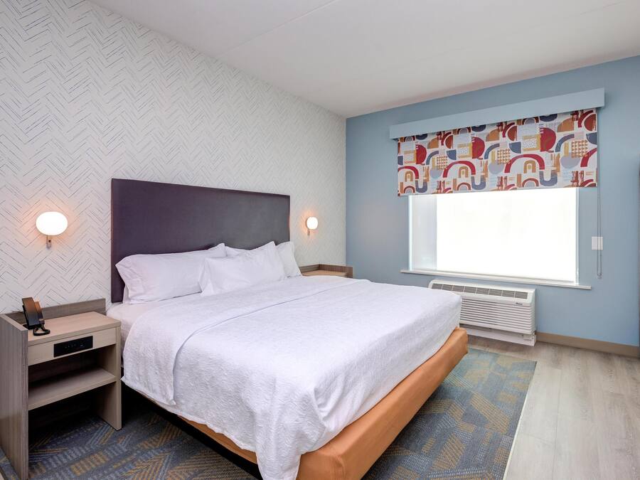 Quarto de hotel bem arrumado, com cama, mesa de cabeceira e janela com cortina.