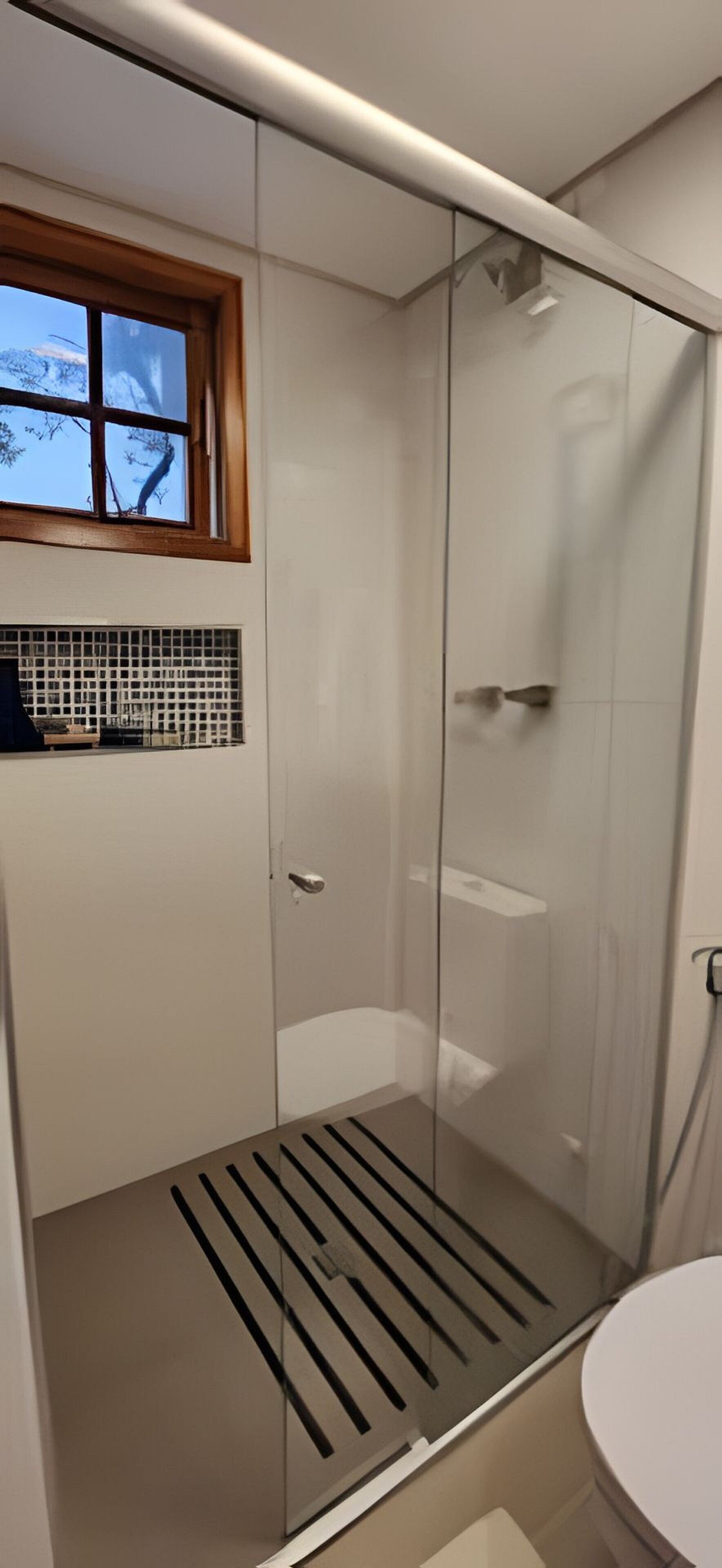 Um banheiro moderno com box de vidro, janela com vista e vaso sanitário branco.