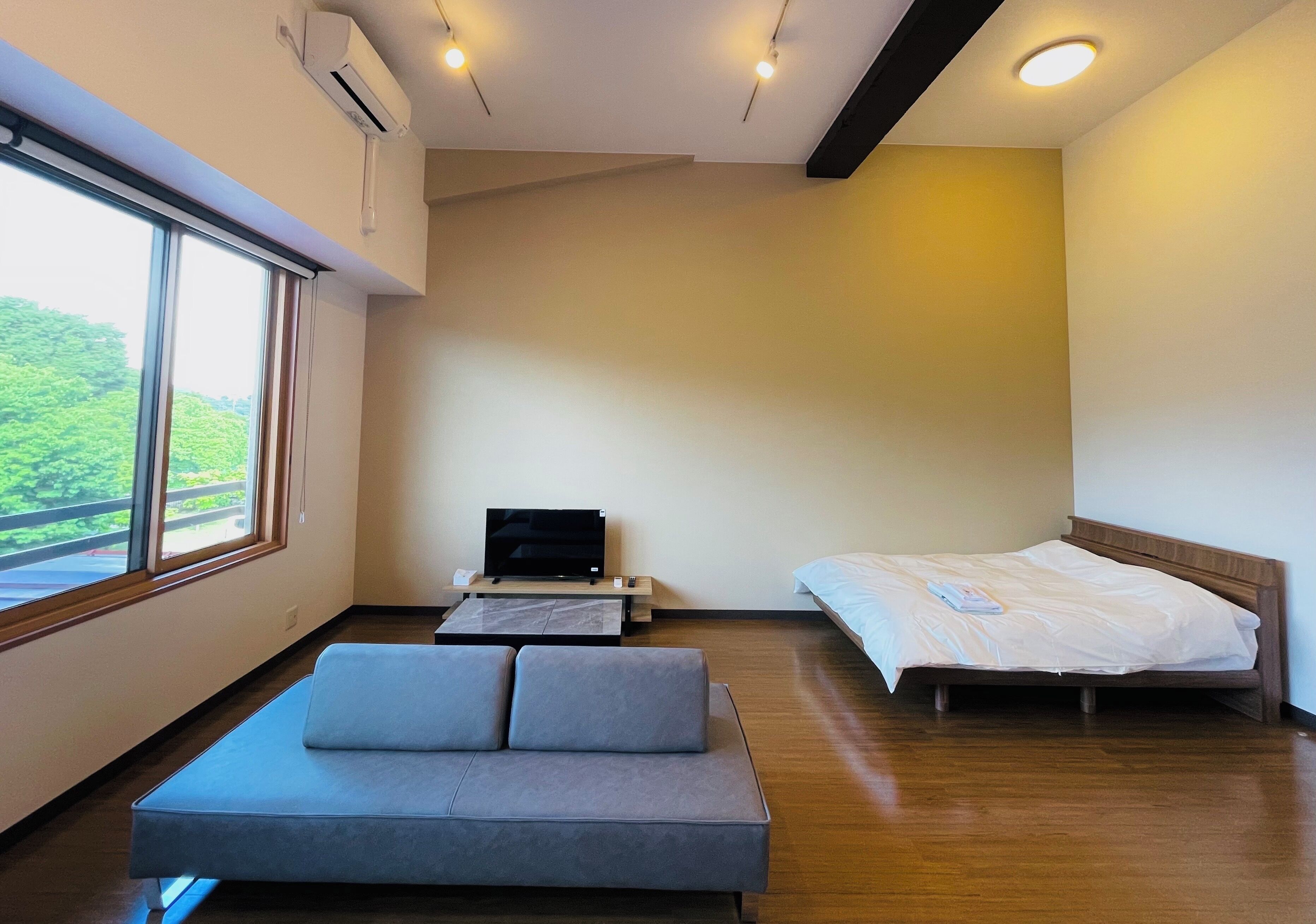Quarto moderno com sofá, cama, televisão e janela com vista para áreas verdes.