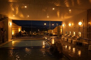 Piscina coberta aquecida com vista para o céu noturno, cercada por áreas de estar e uma parede de bambu.