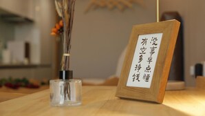 Uma mesa de madeira com uma garrafa de vidro transparente e um quadro com caracteres chineses.