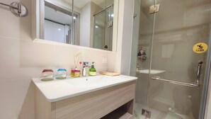 Um banheiro moderno com box de vidro, pia branca e diversos produtos de higiene pessoal, além de um espelho sobre a pia.