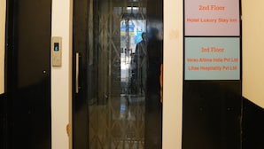 Um elevador com porta de vidro e placa indicando os 1º, 2º e 3º andares, juntamente com os nomes do hotel e das empresas de hospitalidade.