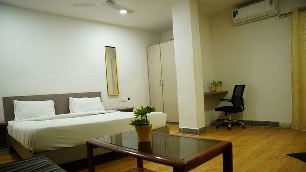 Quarto de hotel com cama, uma mesinha, uma cadeira, escrivaninha e guarda-roupa.