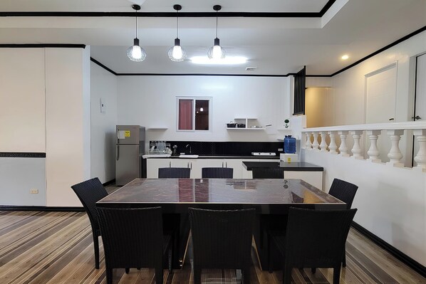 Cozinha moderna com área de refeições, destacando uma mesa grande, cadeiras pretas e iluminação pendente.