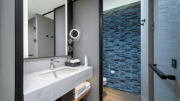 Casa de banho moderna com um espelho grande, lavatório branco e área de duche em azulejo azul.