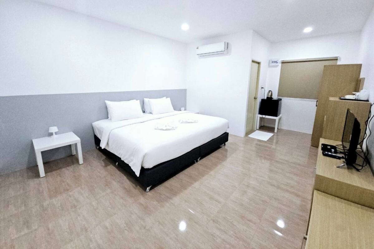 Quarto de hotel moderno com uma cama grande, uma mesinha de cabeceira, uma escrivaninha e um espelho.