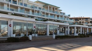 Hotel com vários andares, varandas de vidro, entrada coberta e vista para o porto de iates.