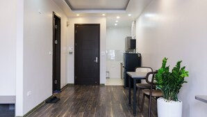 Um corredor com chão de madeira escura, parede branca, porta preta e uma pequena mesa com uma cadeira e um vaso de planta.