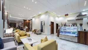 Um saguão de hotel com sofás amarelos, um balcão de recepção e uma vitrine com bebidas.