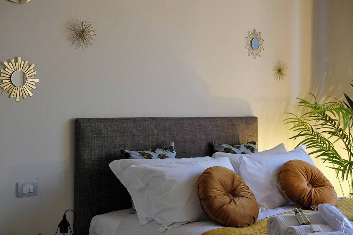 Cama bem arrumada com travesseiros brancos e castanhos, cabeceira cinzenta e arte decorativa na parede.