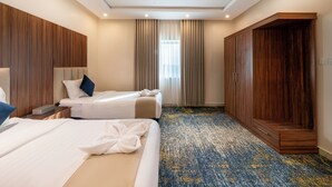 Quarto de hotel com duas camas, um guarda-roupa e uma janela grande com cortinas.