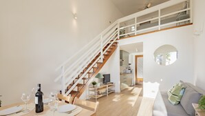 Um espaço de estar moderno com área de jantar, escada, sofá e cozinha.