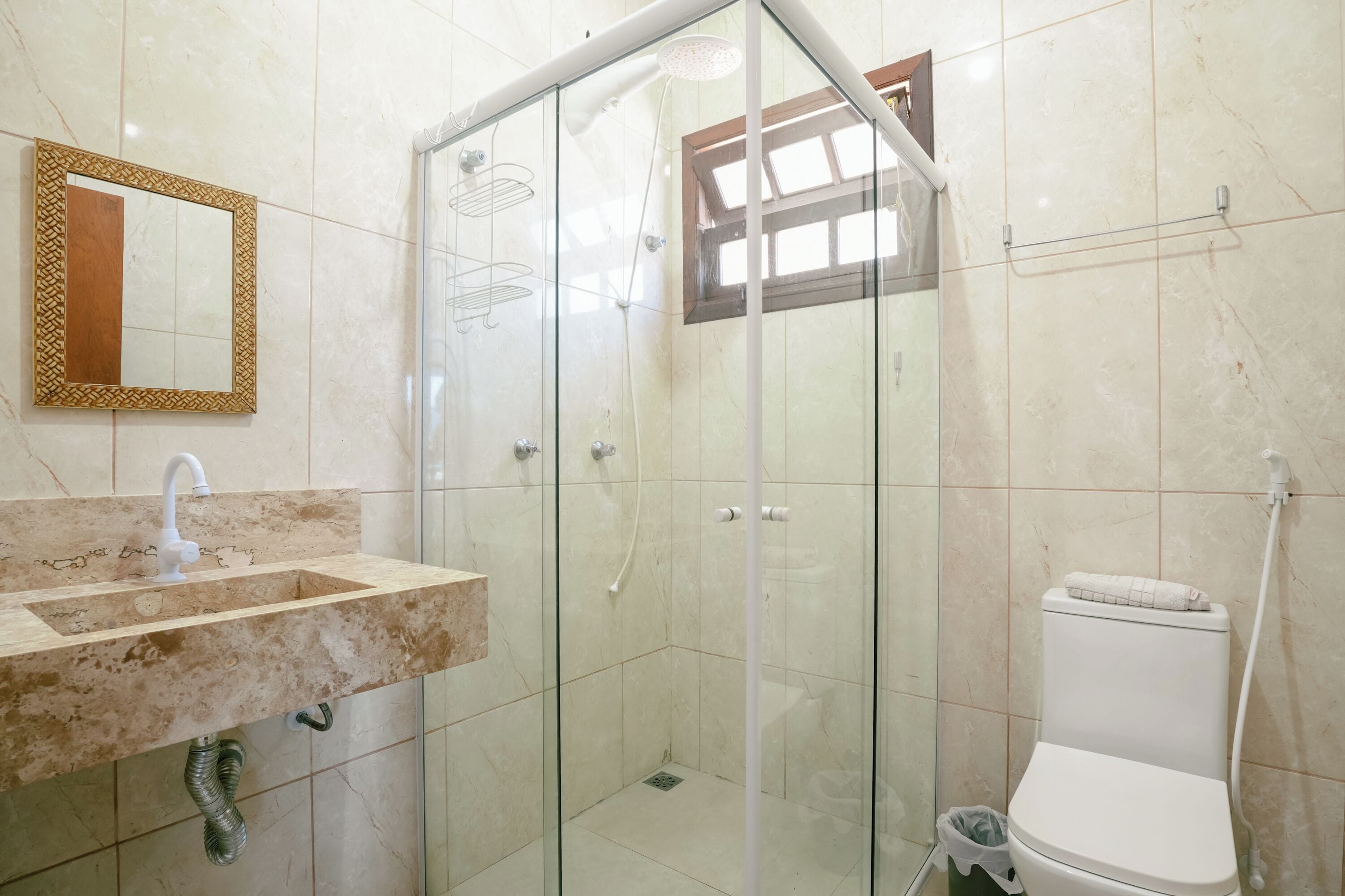 Casa de banho com cabine de duche em vidro, lavatório com bancada de mármore e sanita.